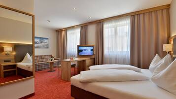 Quarto de hotel com uma cama grande, uma mesa de trabalho, uma televisão e um sofá.