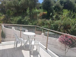 Um terraço com guarda-corpo de vidro, cadeiras de plástico branco e uma mesa redonda.