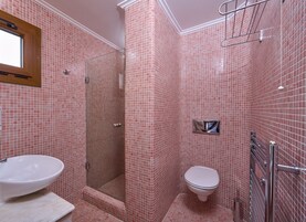 Casa de banho com chuveiro, sanita e lavatório, tudo revestido com um padrão cor-de-rosa.