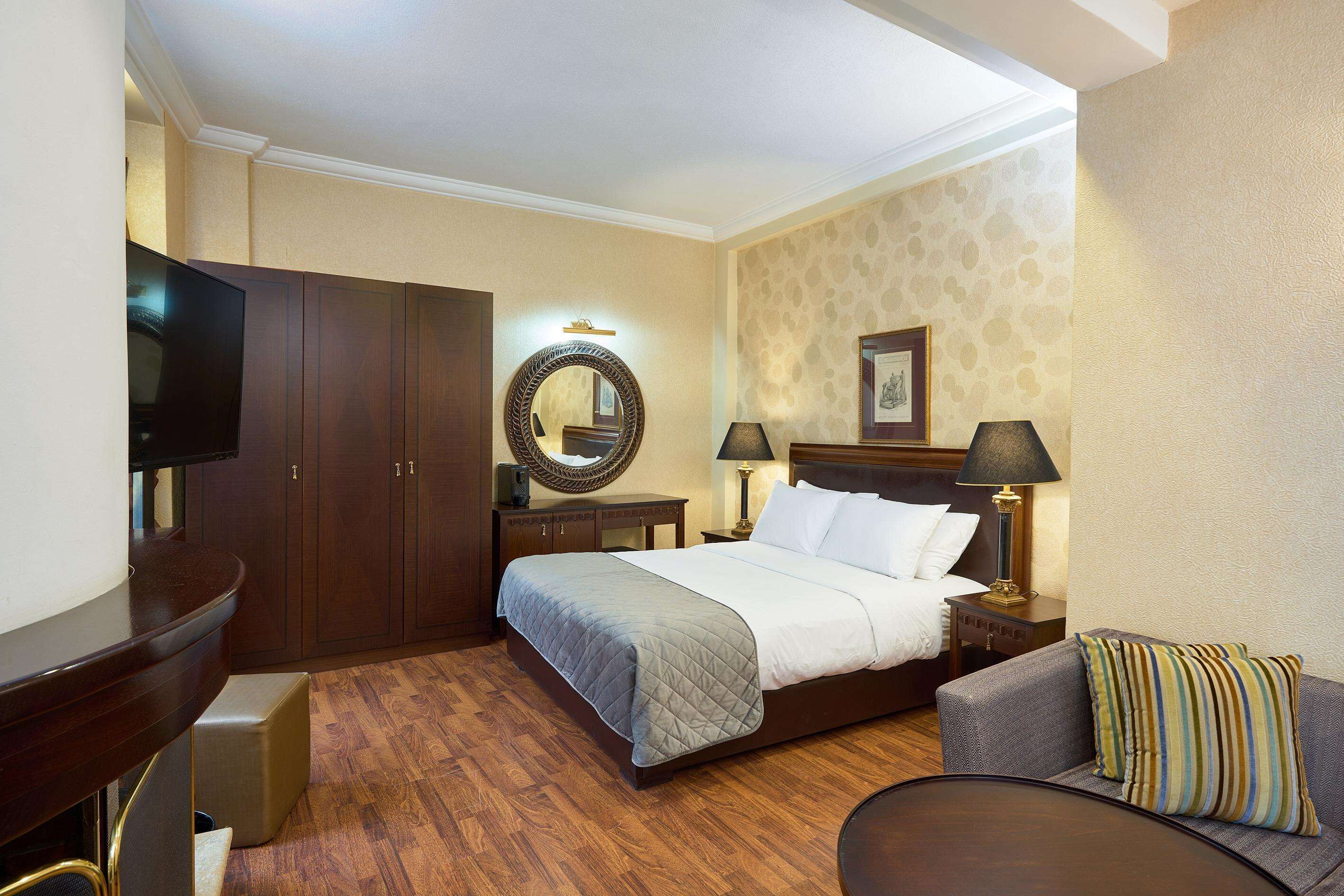 Quarto de hotel com cama, televisão, escrivaninha, cadeira e abajur.