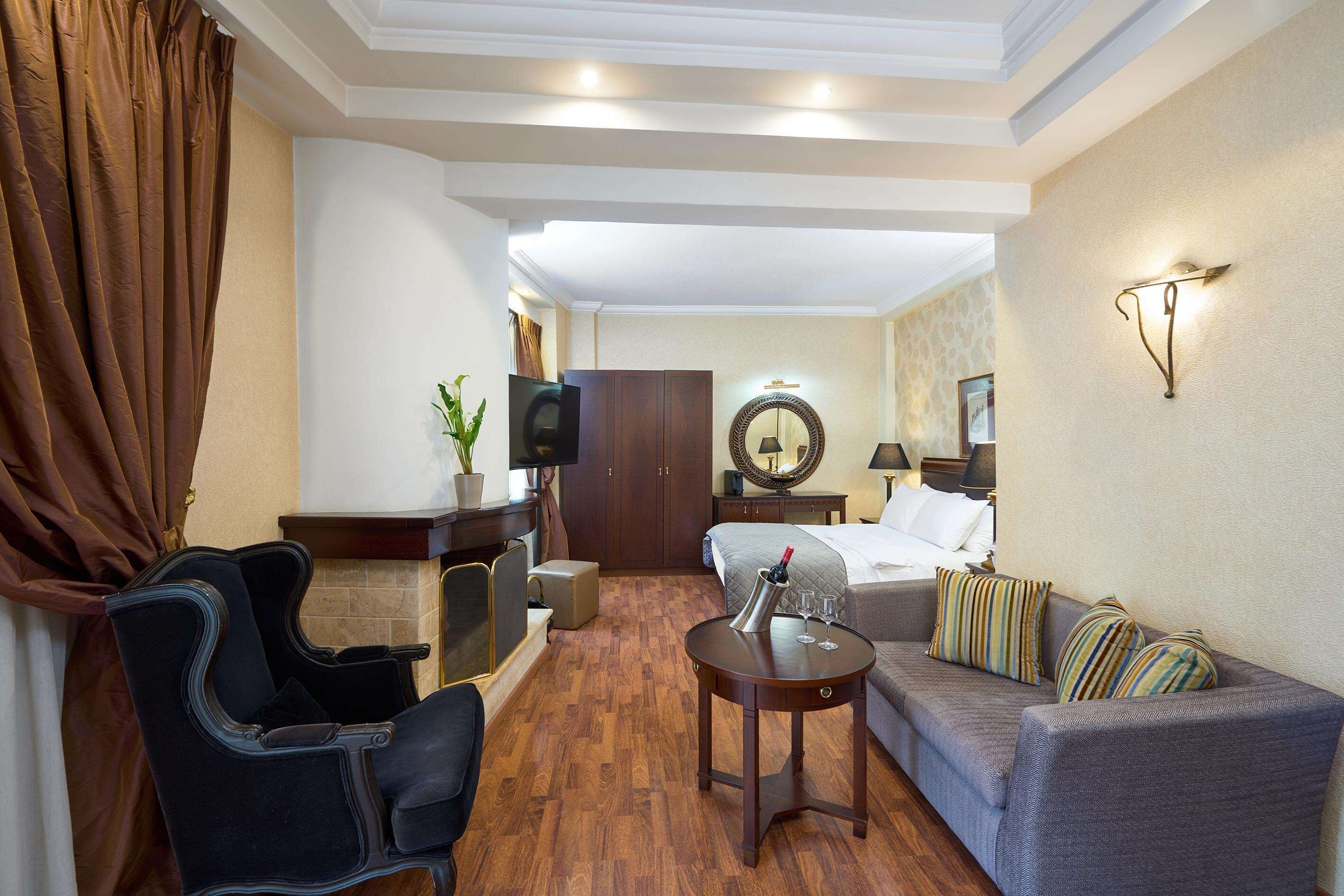 Quarto de hotel com sofá, poltrona, televisão e uma pequena mesa com uma garrafa e copos.