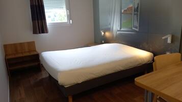 Quarto com cama, um banco de madeira, uma mesa e uma janela com persianas.