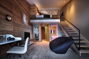 Um espaço de estar moderno estilo loft, com cama em mezzanine, escada, área de refeições com mesa e cadeiras brancas e um canto de estar aconchegante com um bean bag.