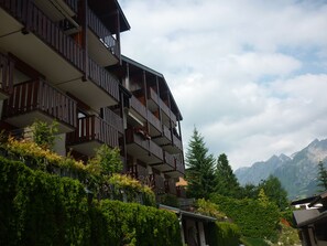 Um edifício com vários andares e varandas, rodeado por vegetação exuberante e montanhas ao fundo.