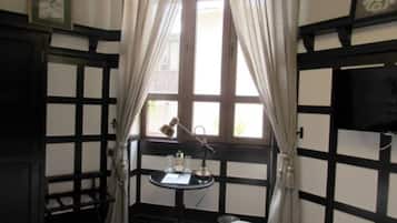 Um quarto com uma cama, uma escrivaninha com abajur e uma janela com cortinas.