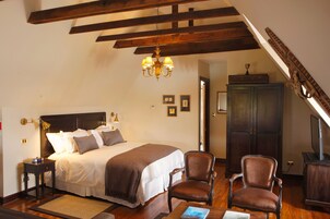 Quarto com uma cama grande, duas cadeiras, um armário de madeira e um candelabro.