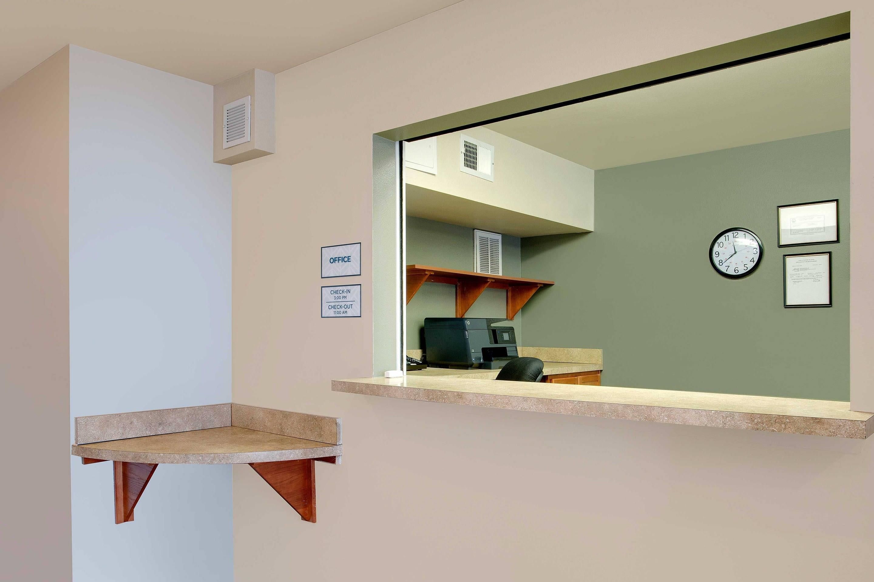 Um espaço de escritório pequeno com uma mesa, um computador e um relógio na parede.