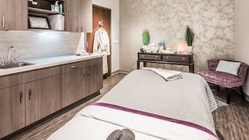 Quarto de hotel moderno com cama, pequena escrivaninha, toucador com espelho e banheiro com pia e porta-toalhas.