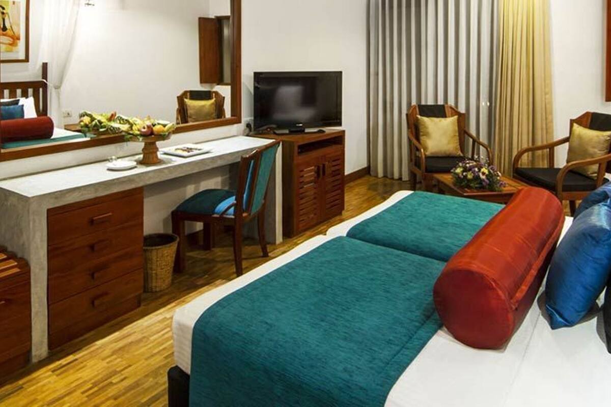 Quarto de hotel com cama, escrivaninha, cadeira, televisão e cortinas.