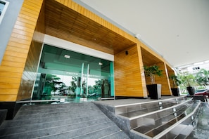 Entrada de hotel moderna com fachada de madeira, portas de vidro e escadaria que leva ao saguão.