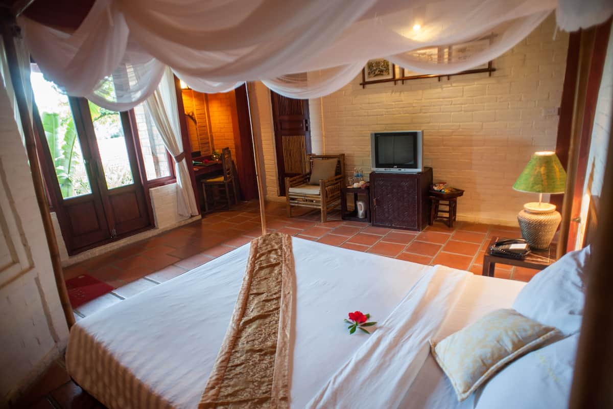 Quarto de hotel com cama, televisão, uma pequena mesa e abajur.