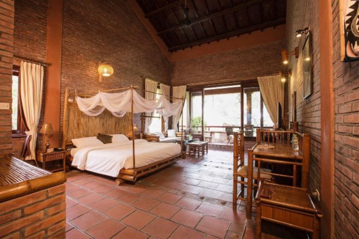 Um quarto espaçoso com uma cama grande, uma escrivaninha de madeira e uma varanda com vista.