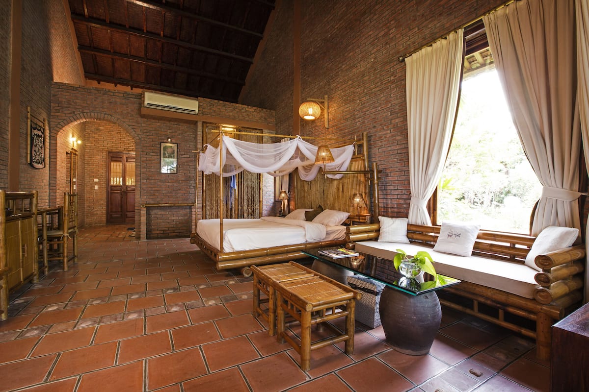 Quarto com cama, sofá, mesa e janela com cortinas.
