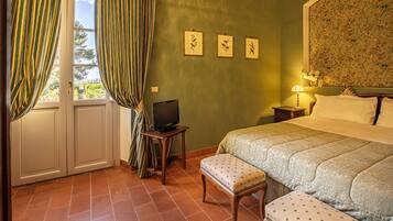 Quarto de hotel com uma cama, televisão, um banco, mesa de cabeceira com abajur e três quadros na parede.