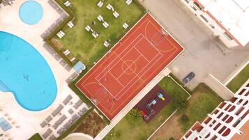 Vista aérea de uma instalação esportiva com quadra de basquete, piscina e quadra de tênis.