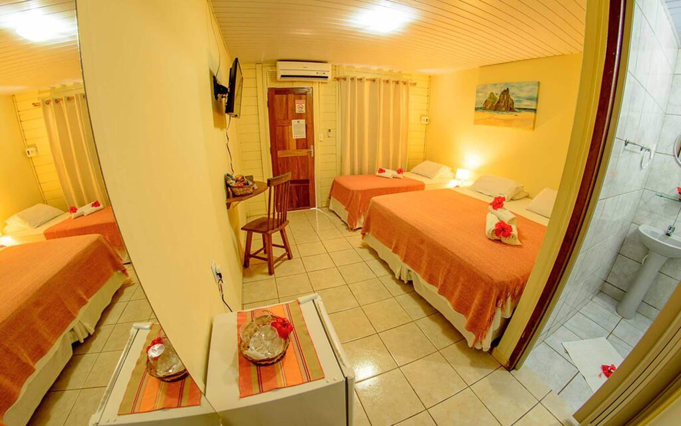 Quarto de hotel com duas camas, uma escrivaninha, uma cadeira e um banheiro.