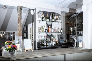 Uma área de bar com prateleiras de garrafas de bebidas, um caixa registradora e um vaso de flores.