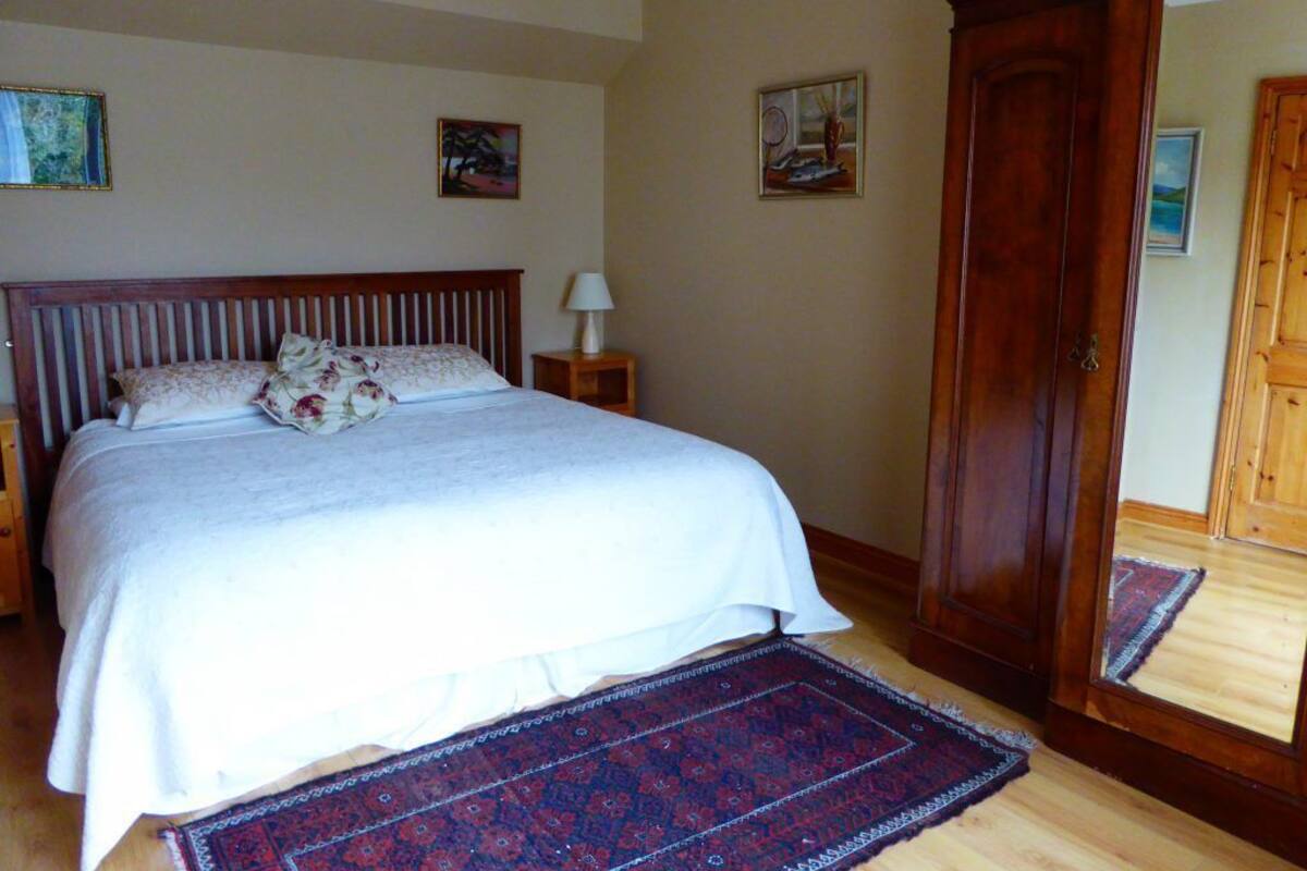 Quarto com cama, mesa de cabeceira, abajur, guarda-roupa de madeira e tapete.
