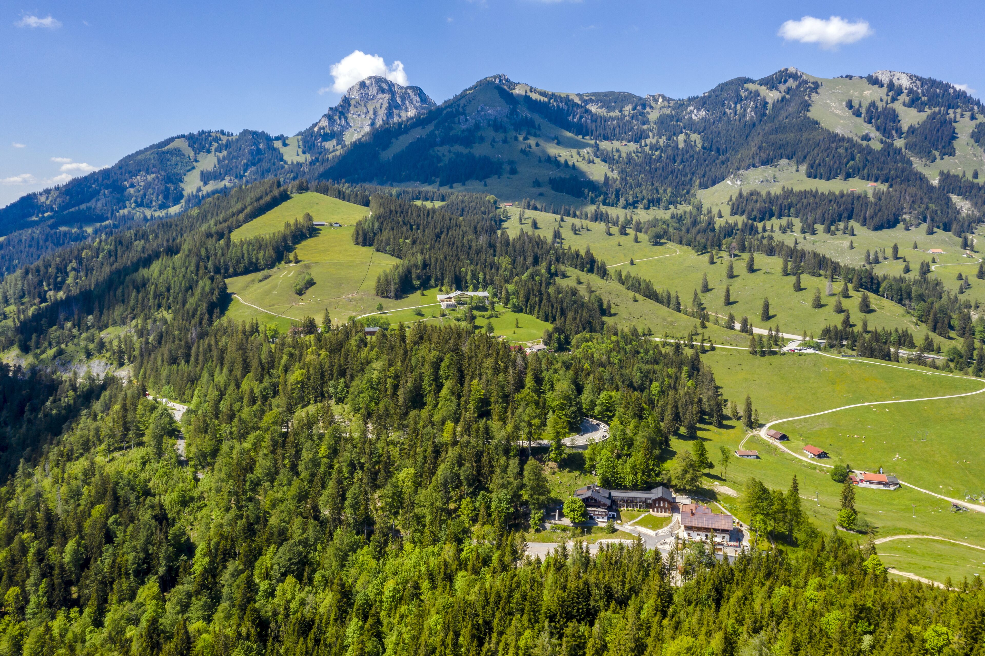 Paisagem montanhosa com um grande edifício cercado por florestas densas e clareiras.
