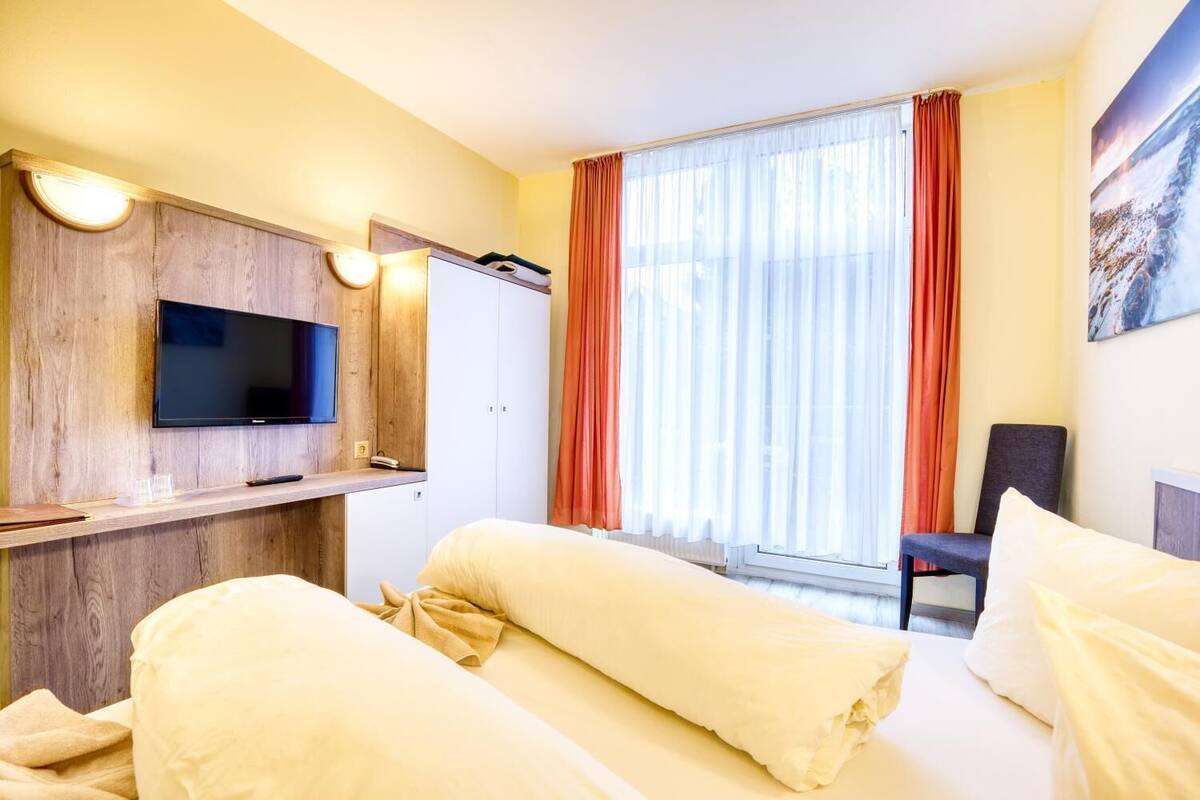 Quarto de hotel com cama, televisão, escrivaninha e janela com cortinas.
