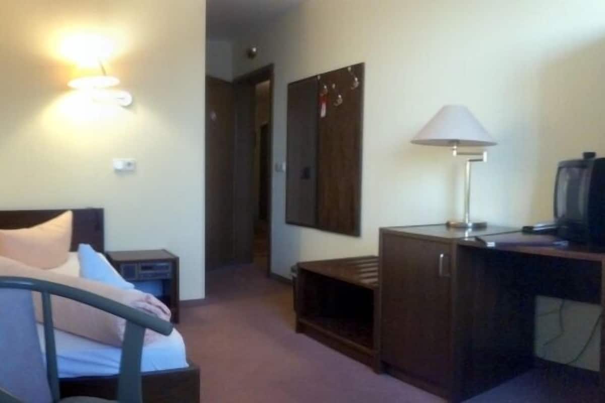 Quarto de hotel com uma cama, escrivaninha com abajur, televisão e guarda-roupa.