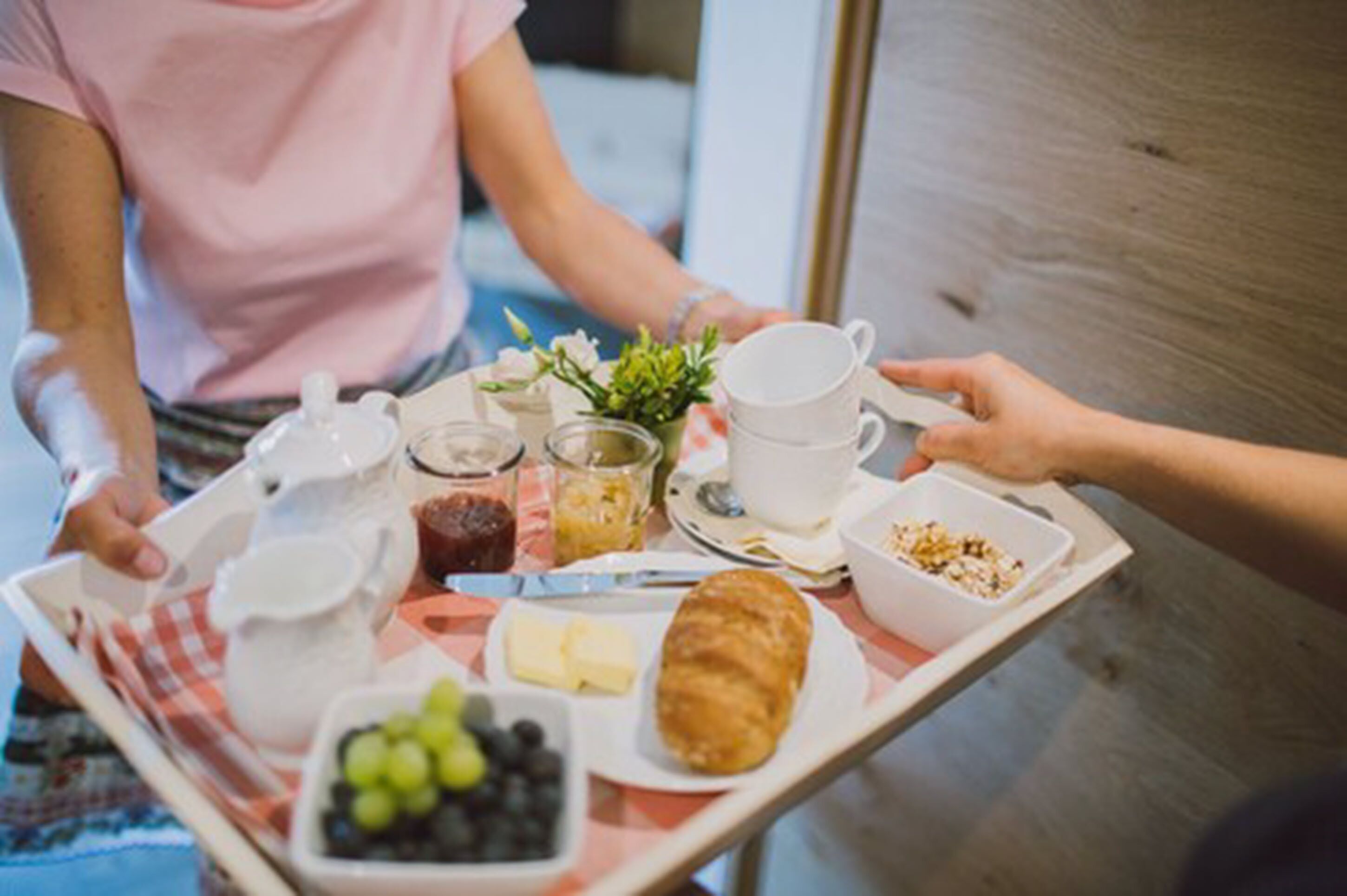 Uma bandeja com itens de café da manhã, incluindo um croissant, uvas, manteiga, geleia e uma xícara.