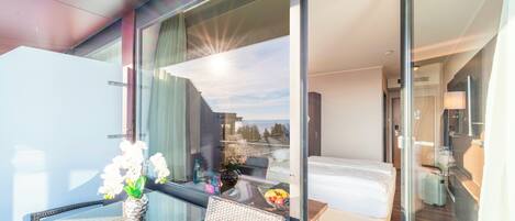 Quarto de hotel moderno com varanda, cama, uma pequena mesa com um vaso de flores e vista para o exterior.