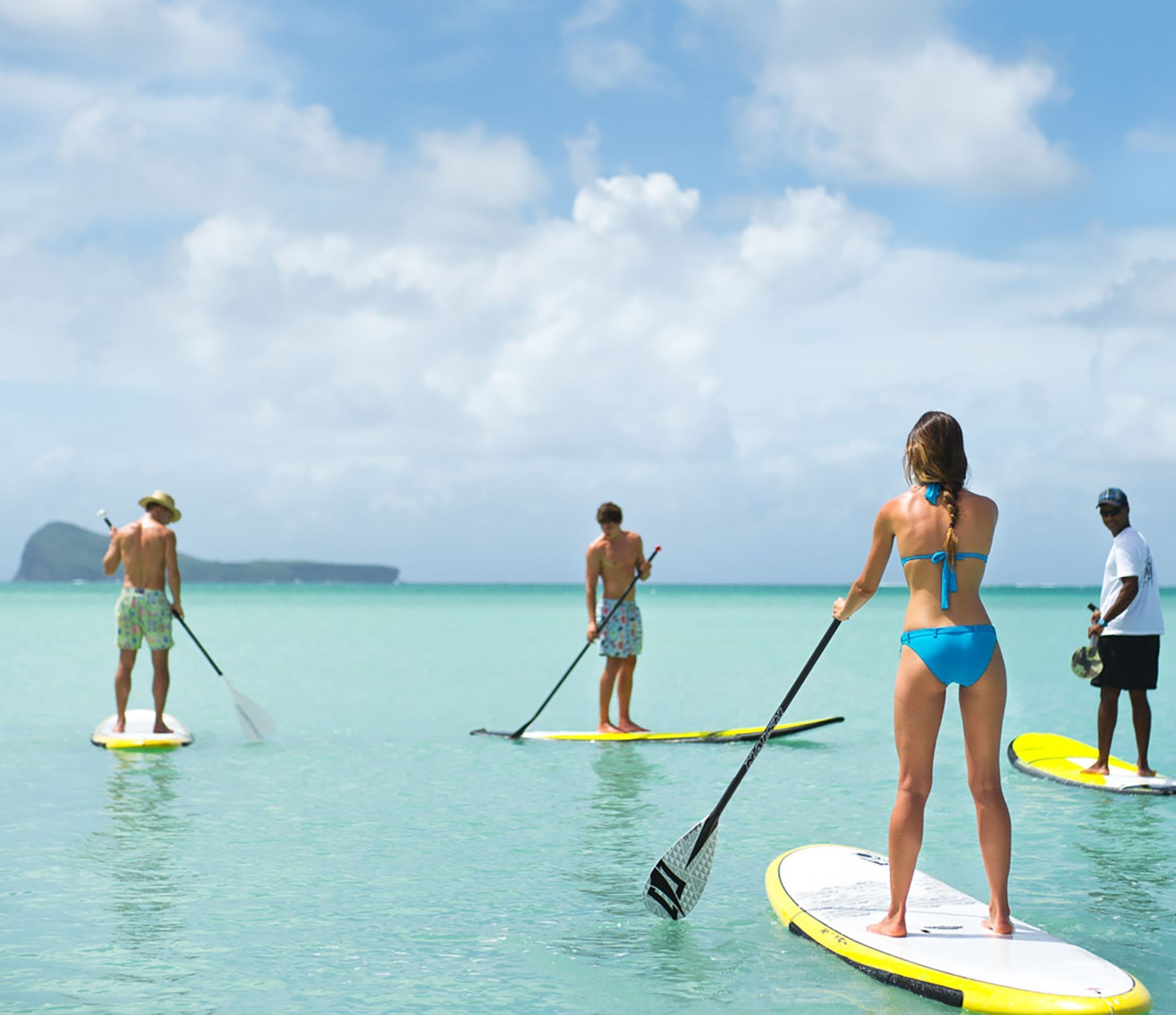 Pessoas praticando paddleboard em um mar calmo, sob céu claro.