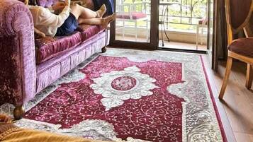 Quarto com sofá roxo, cadeira de madeira e tapete estampado.