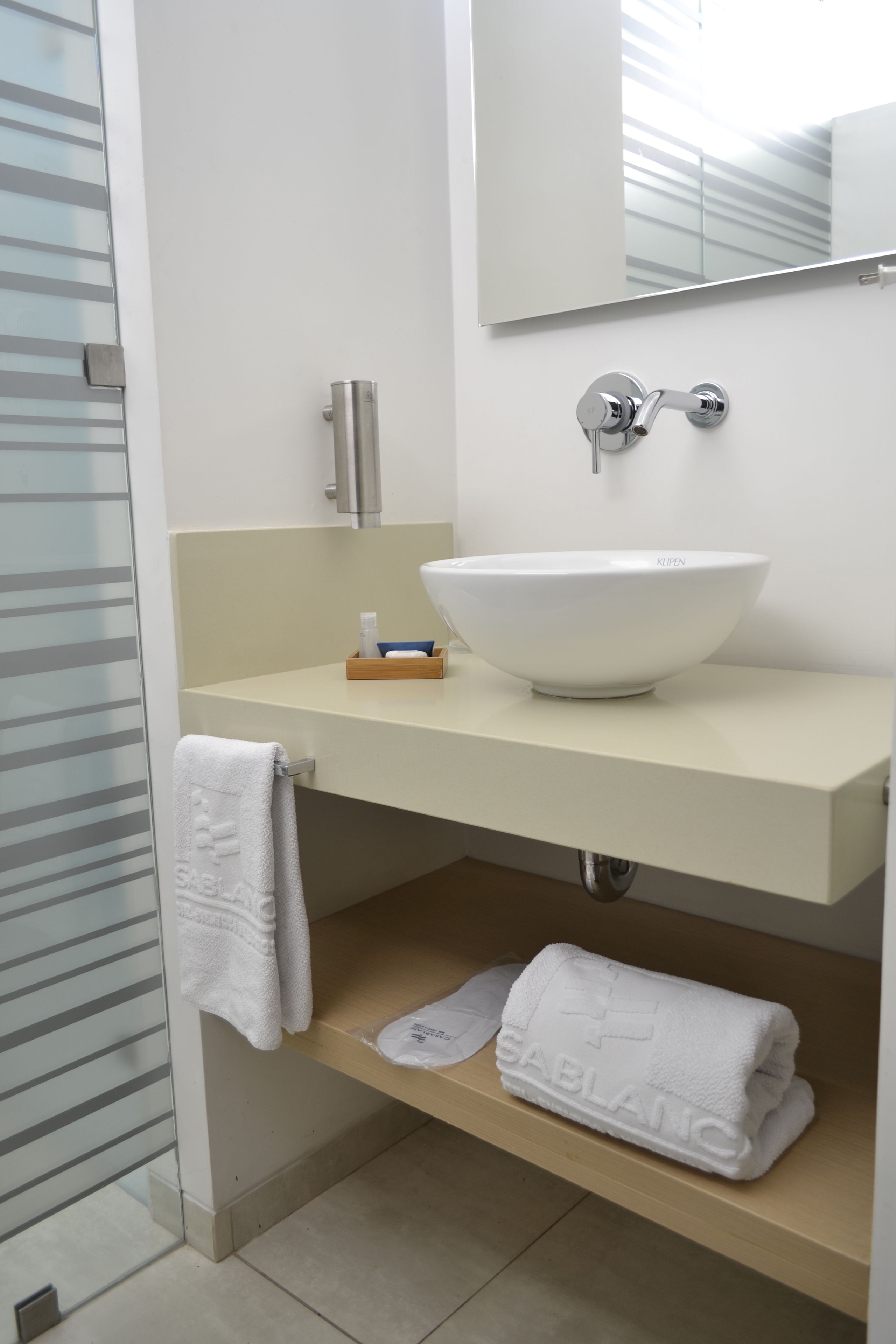 Casa de banho moderna com lavatório branco, espelho e porta-toalhas.
