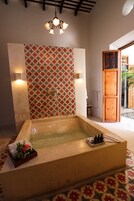 Uma área de spa com uma banheira grande, azulejos decorativos na parede e uma porta de madeira que dá para outro quarto.