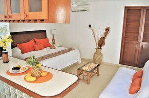 Quarto de hotel com cama, mesinha com prato de frutas, sofá e armários de madeira.