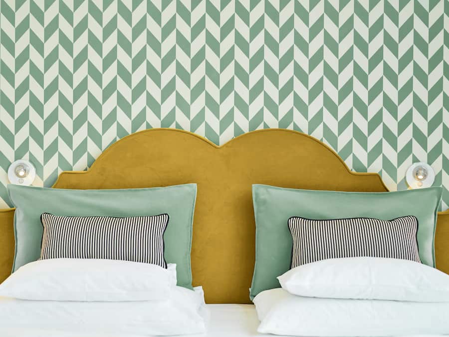 Cama com cabeceira, duas almofadas e parede com padrão em chevron.