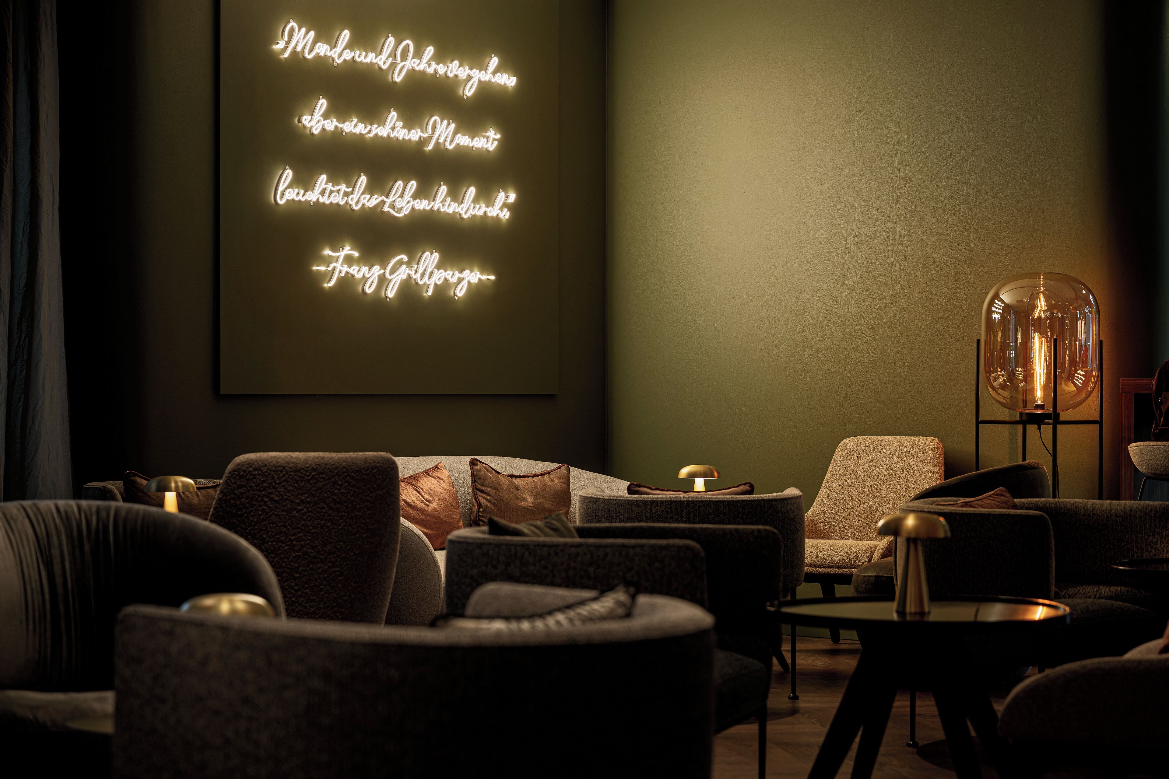 Uma área de estar com iluminação suave, um letreiro de neon, assentos confortáveis e uma mesa com luminária.