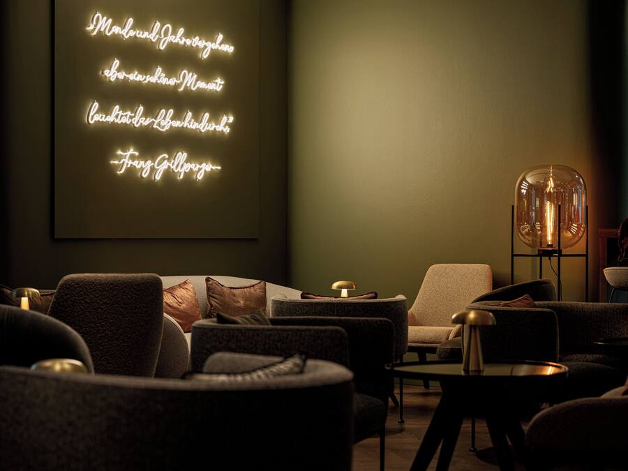 Uma área de estar com iluminação suave, um letreiro de neon, assentos confortáveis e uma mesa com luminária.