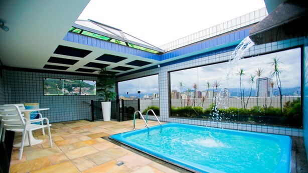 Piscina no terraço com vista para a paisagem urbana, área de estar com cadeiras e piso revestido de azulejos.