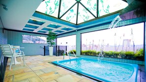 Piscina interna com vista para a paisagem urbana, paredes azulejadas e teto com claraboias.