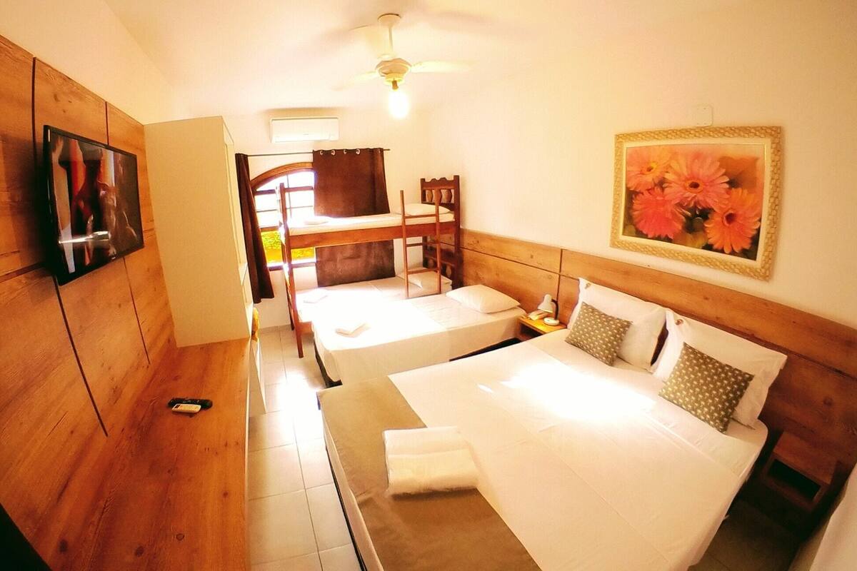 Um quarto com beliches, uma cama com almofadas, uma mesa de cabeceira com abajur e um quadro na parede.