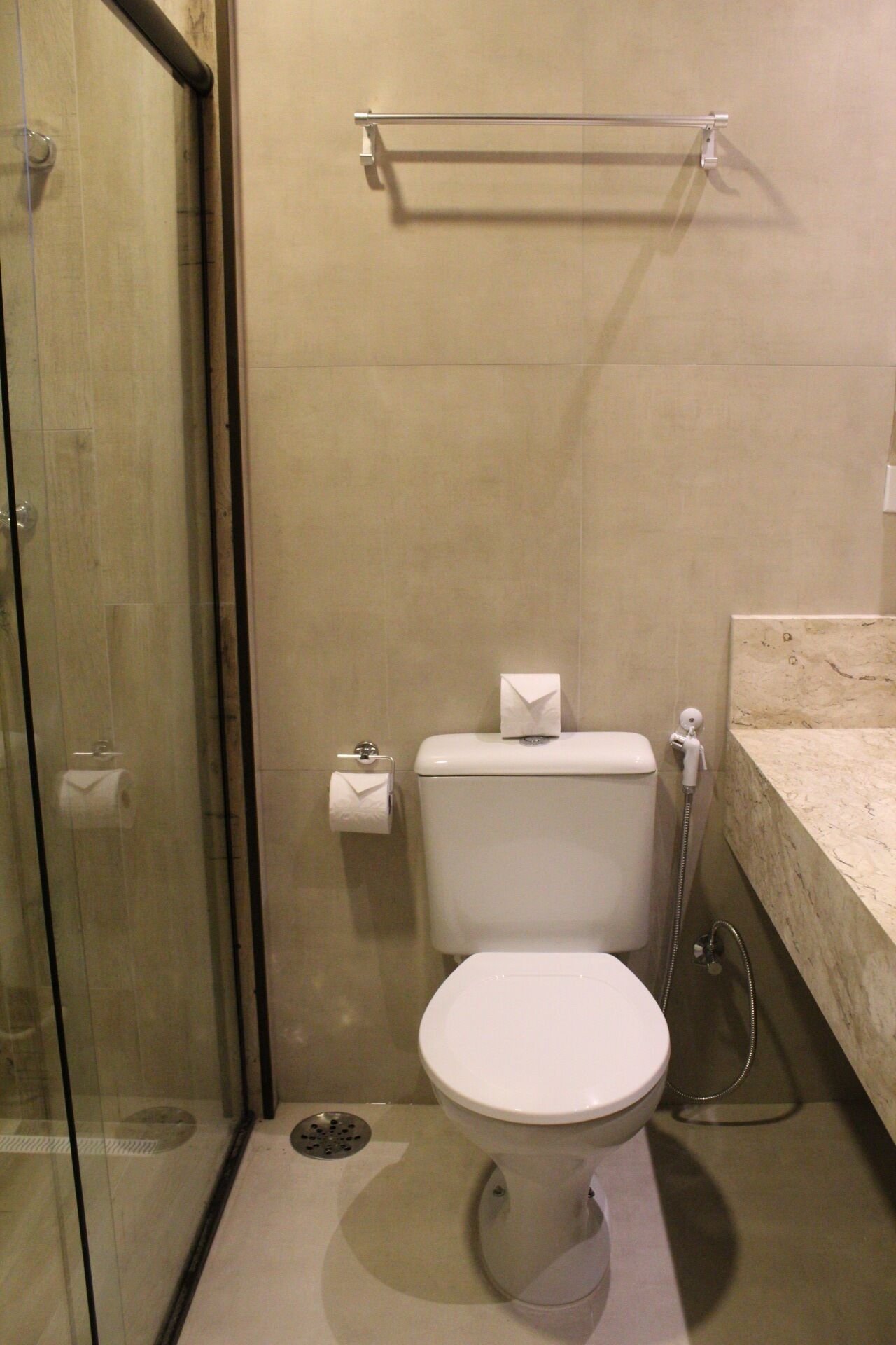 Um banheiro pequeno com vaso sanitário, box de chuveiro em vidro e bancada de mármore.