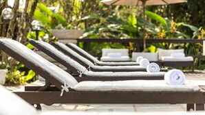 Fileira de espreguiçadeiras com toalhas, um deck de madeira e um grande guarda-sol.