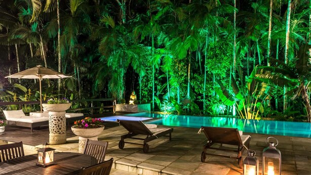Uma área de piscina ao ar livre com espreguiçadeiras, uma mesa e plantas em vasos.