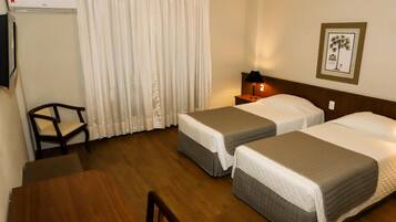 Quarto de hotel com duas camas, uma mesa de madeira, uma cadeira, televisão e um quadro na parede.