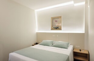 Quarto de hotel com cama, mesas de cabeceira, luminária e um quadro na parede.