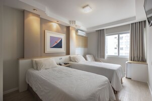 Quarto de hotel com duas camas, ar condicionado fixado na parede, um quadro enquadrado e uma janela com cortinas.