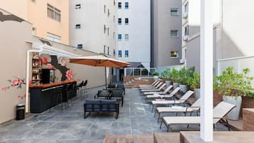 Uma área externa com assentos, um bar, cadeiras de estar e plantas em vasos.