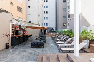 Uma área externa com assentos, um bar, cadeiras de estar e plantas em vasos.