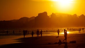 Uma praia com pessoas caminhando pela orla durante o pôr do sol.