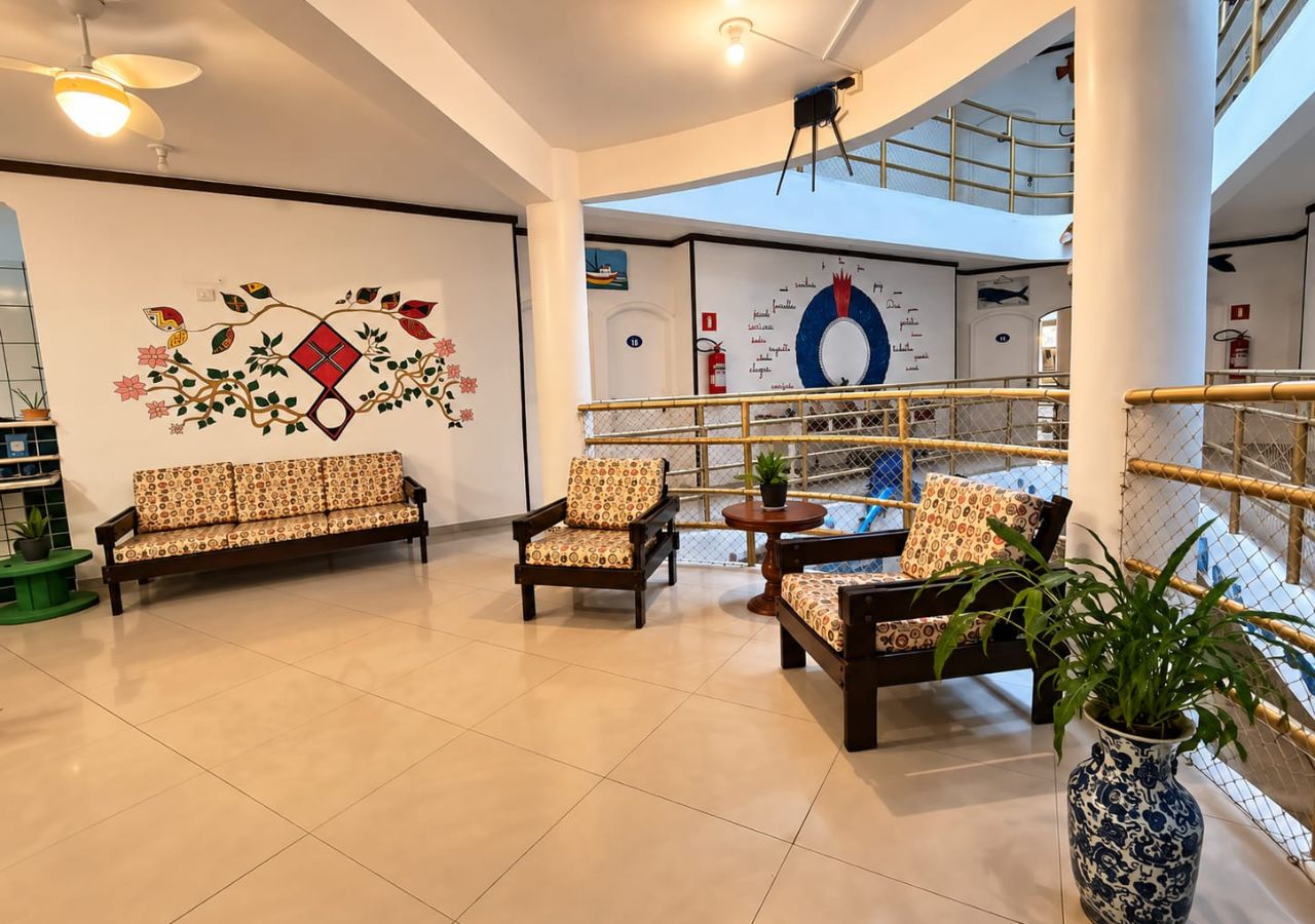 Um hall espaçoso com teto alto, área de estar com sofás e poltronas estampadas, um mural decorativo e vista para o andar superior através de uma balaustrada de vidro.