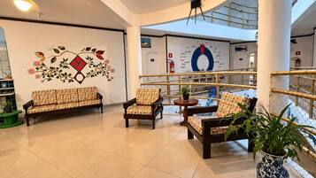 Um hall espaçoso com teto alto, área de estar com sofás e poltronas estampadas, um mural decorativo e vista para o andar superior através de uma balaustrada de vidro.