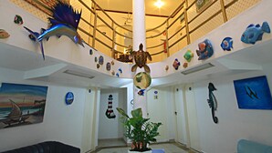 Um átrio em vários níveis com uma escadaria central, arte de parede com peixes decorativos e uma planta em vaso sobre uma mesa redonda.